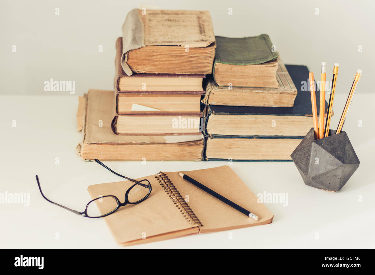 Stack of old books, textbook, glasses and pencils in office background ...