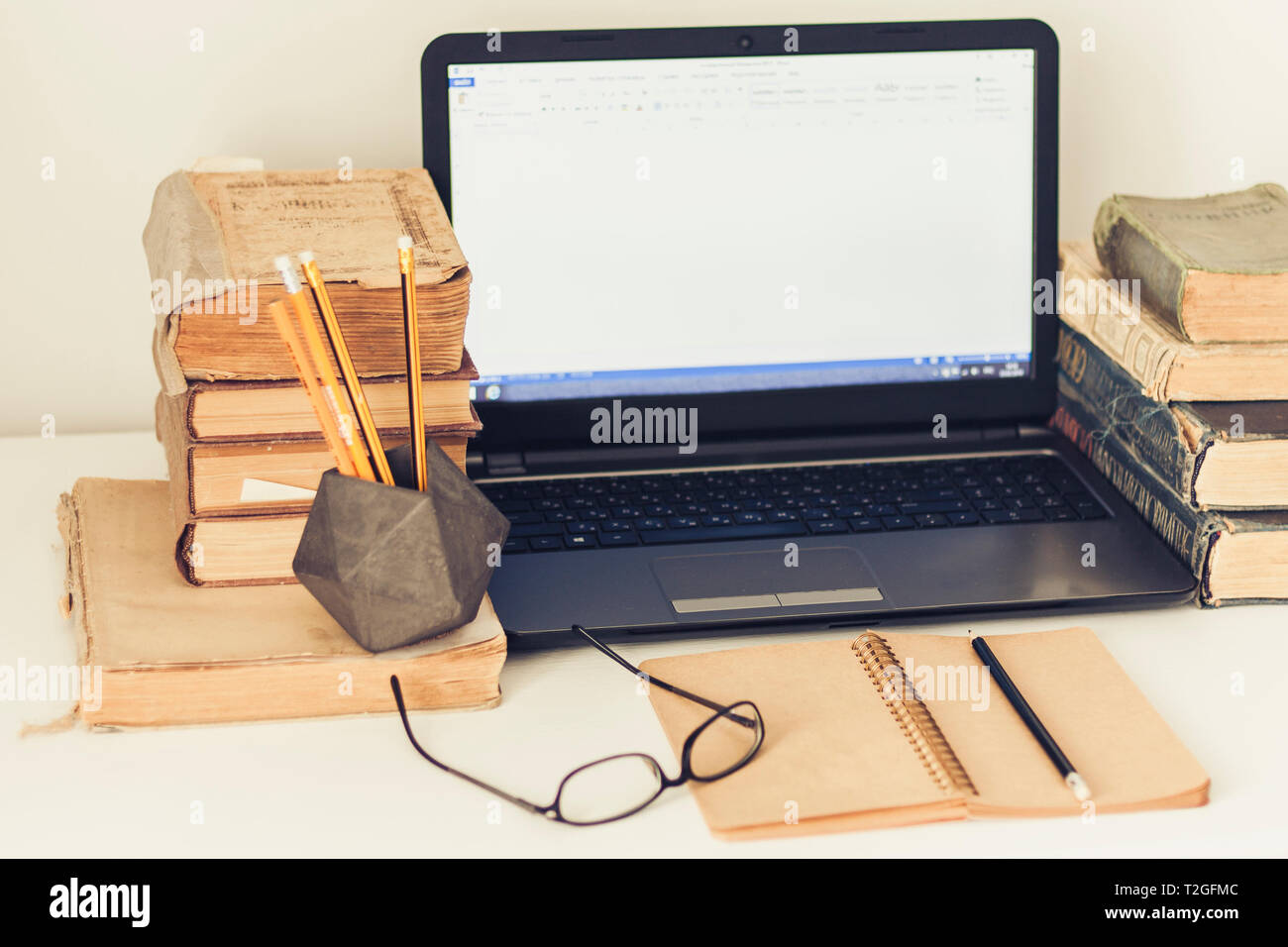 Laptop, stack of old books, notebook and pencils on white table ...