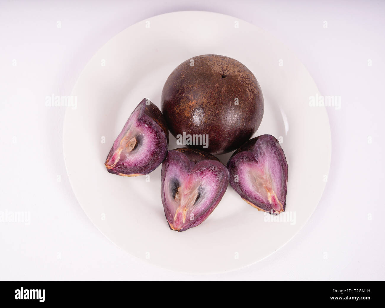 A caimito fruit and three piece of caimito fruit on white plate Stock ...
