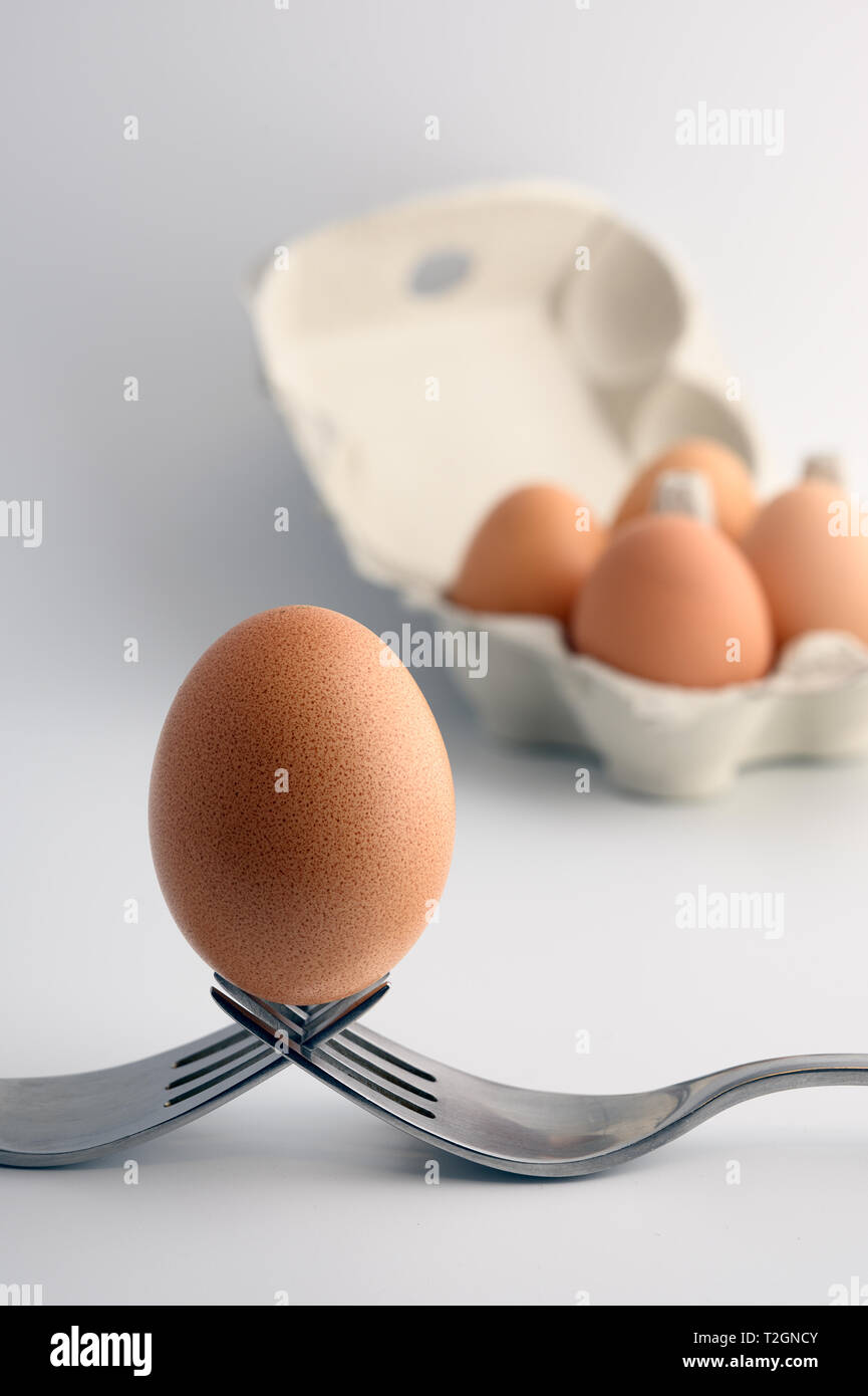 Egg in balance on two forks on white background. Four more eggs out of ...