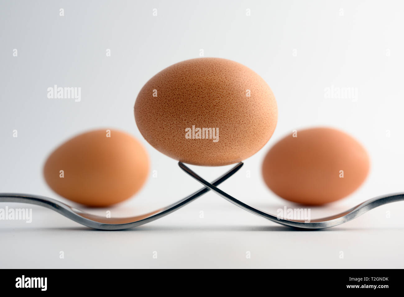 Egg in balance on two forks on white background. Two more eggs out of ...