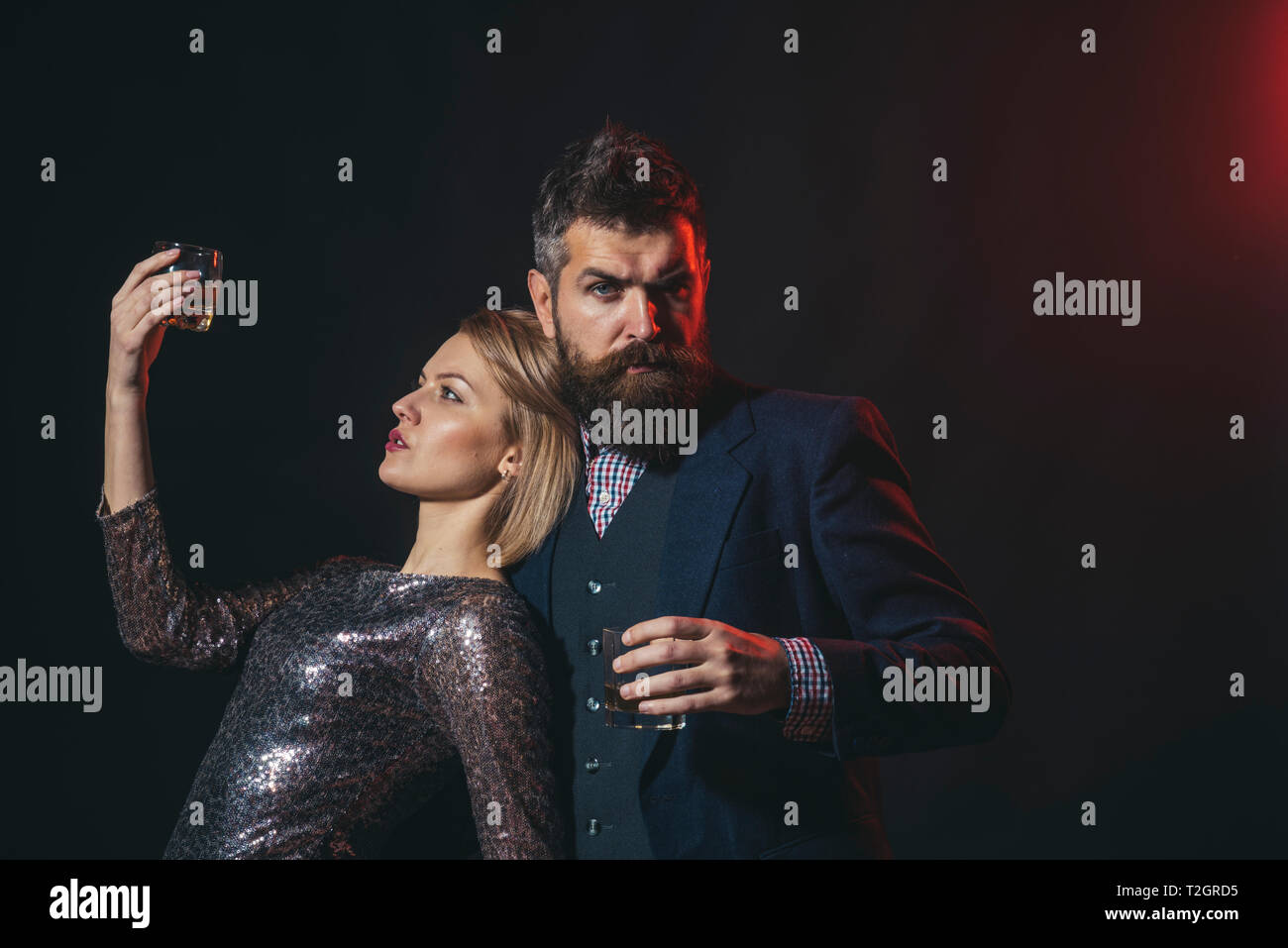 Man and woman in fancy clothes drink wiskey on dark background. Couple ...