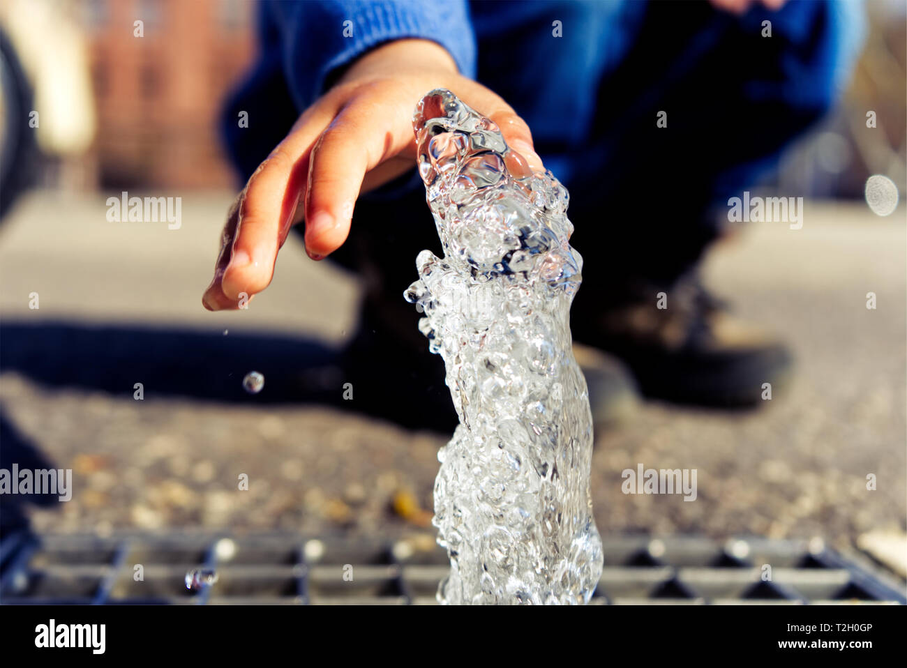 child's hand touching the water from a fountain coming from the ground ...