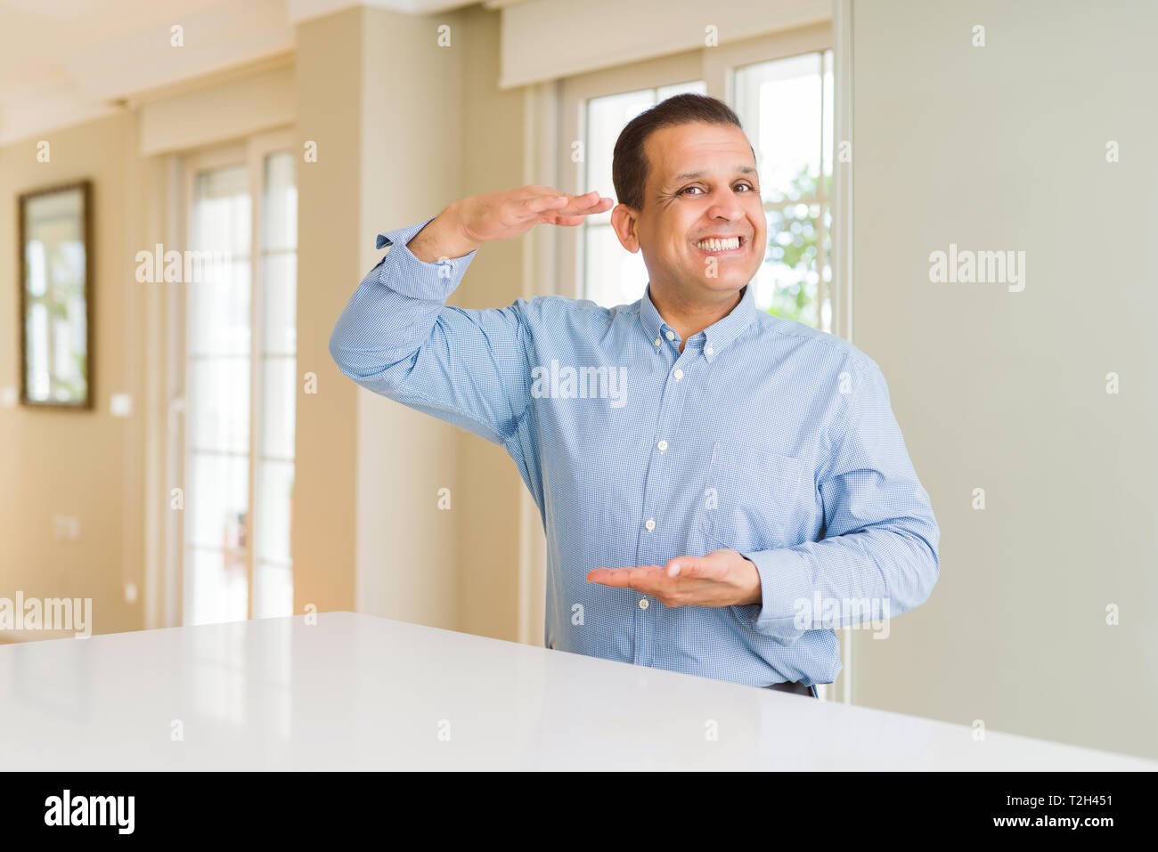 Middle age man sitting at home gesturing with hands showing big and ...