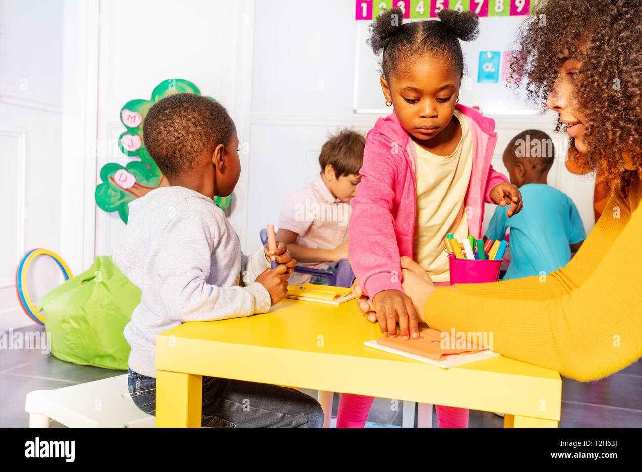 Nursery school class children black boy and girl work with teacher on ...