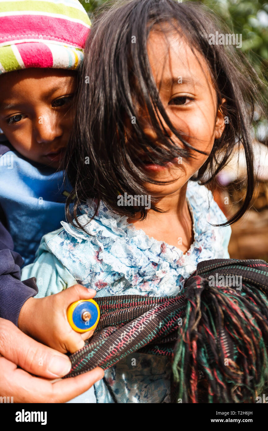 Village girl with hair falling in her face carrying younger child in ...