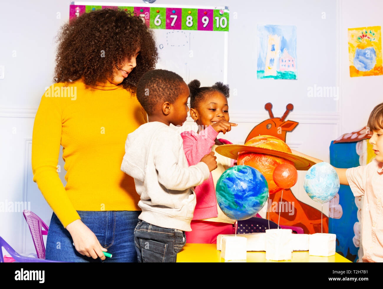 Group of kids in kindergarten play planet models with teacher showing ...