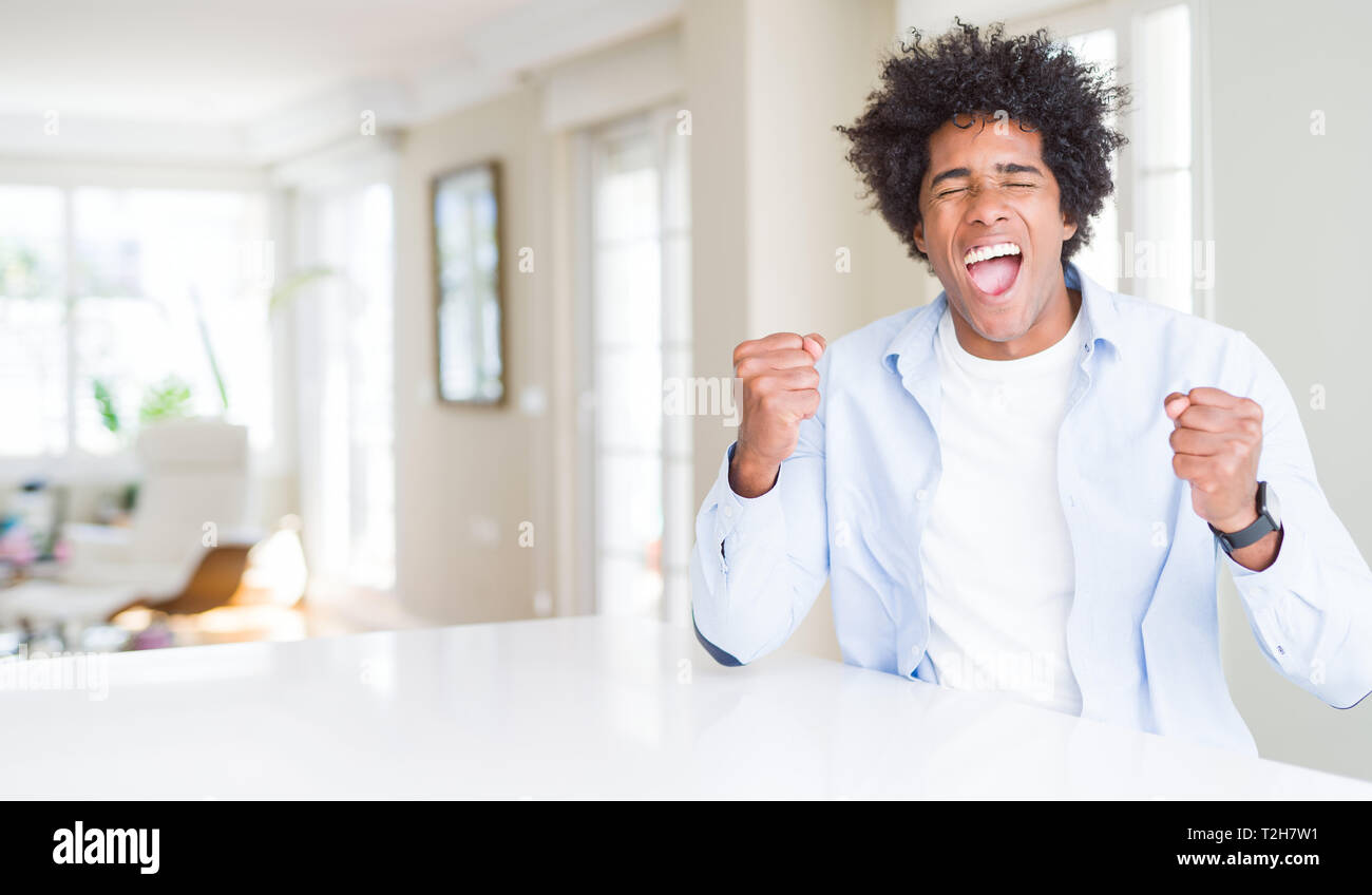 African American man at home excited for success with arms raised ...
