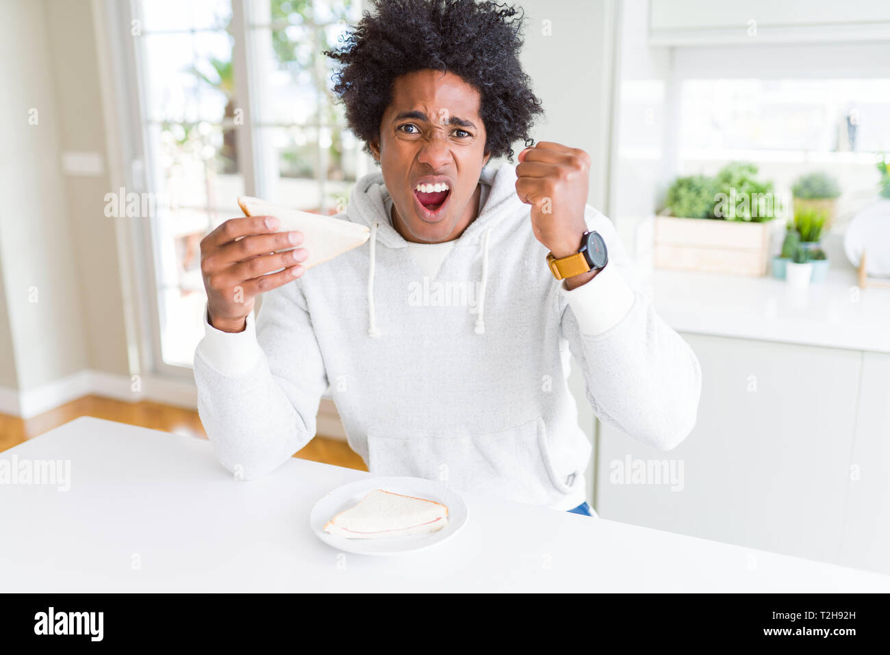 African American man eating handmade sandwich at home annoyed and ...