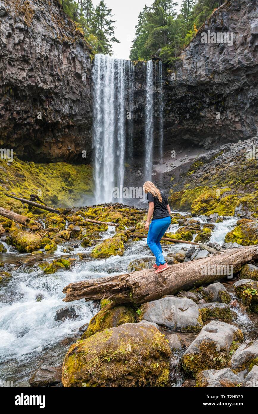 Young woman crosses river, hiker, waterfall flows over rocky outcrop ...