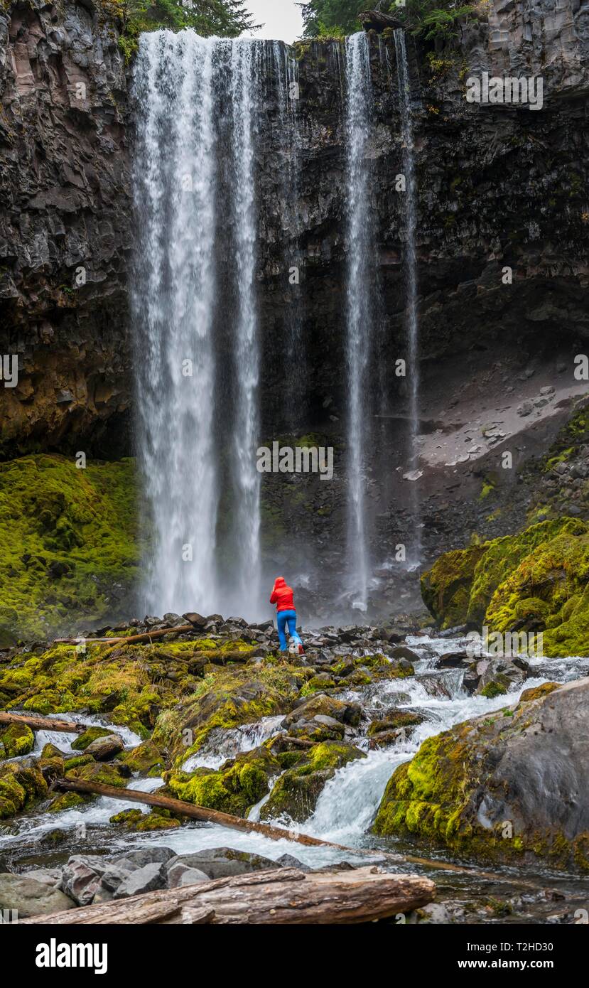 Hiker in front of a high waterfall, water falls over a rocky outcrop ...