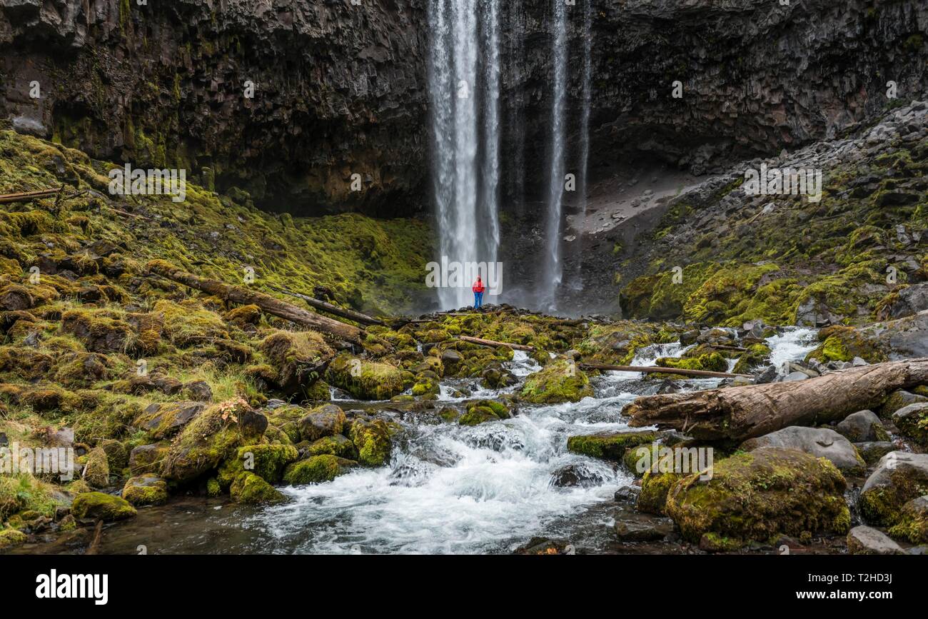 Hiker in front of a high waterfall, water falls over a rocky outcrop ...