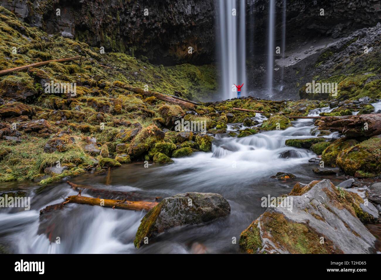 Hiker in front of a high waterfall, water falls over a rocky outcrop ...