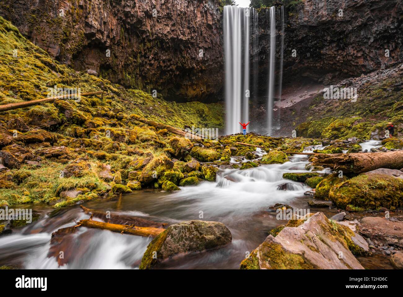 Hiker in front of a high waterfall, water falls over a rocky outcrop ...