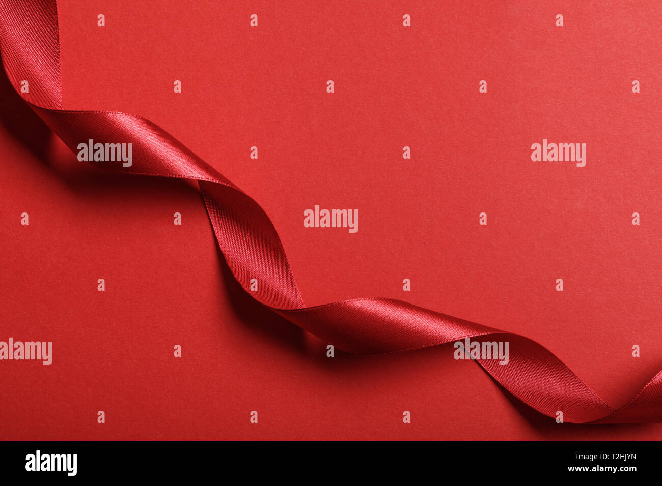 top view of curved silk red ribbon on red background with copy space ...