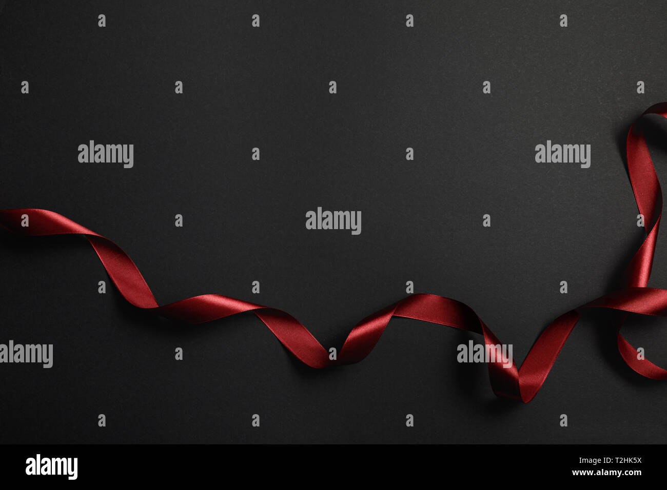 top view of red silk wavy ribbon on black background with copy space ...