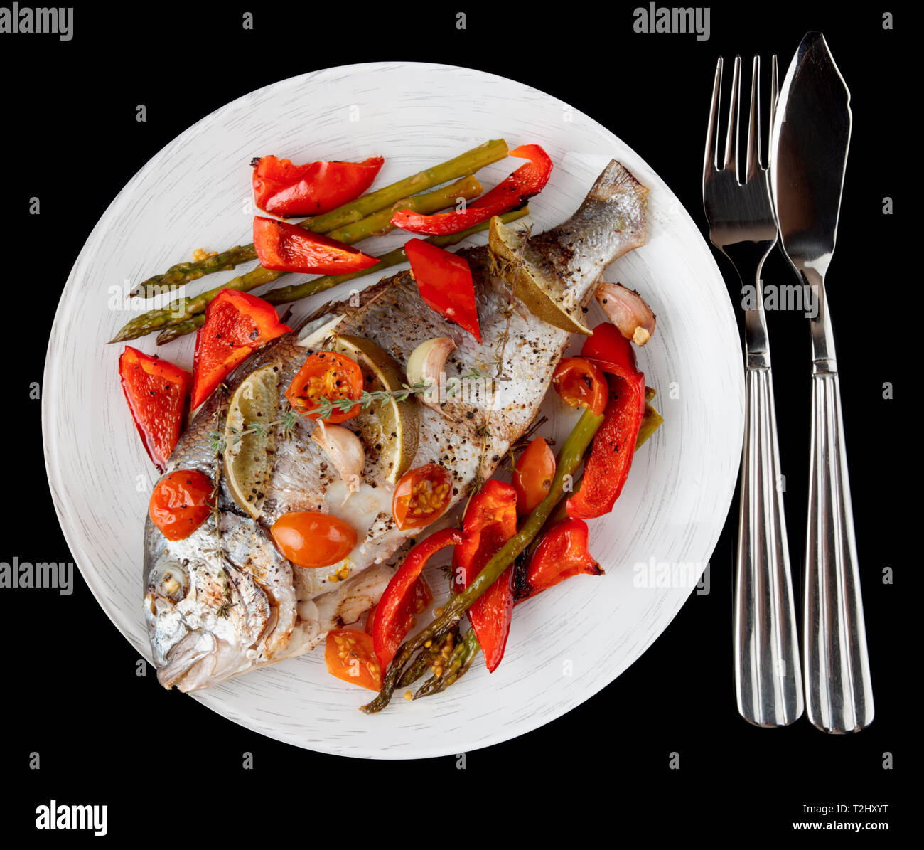 Roasted gilt-head bream with vegetables on plate, isolated on black ...