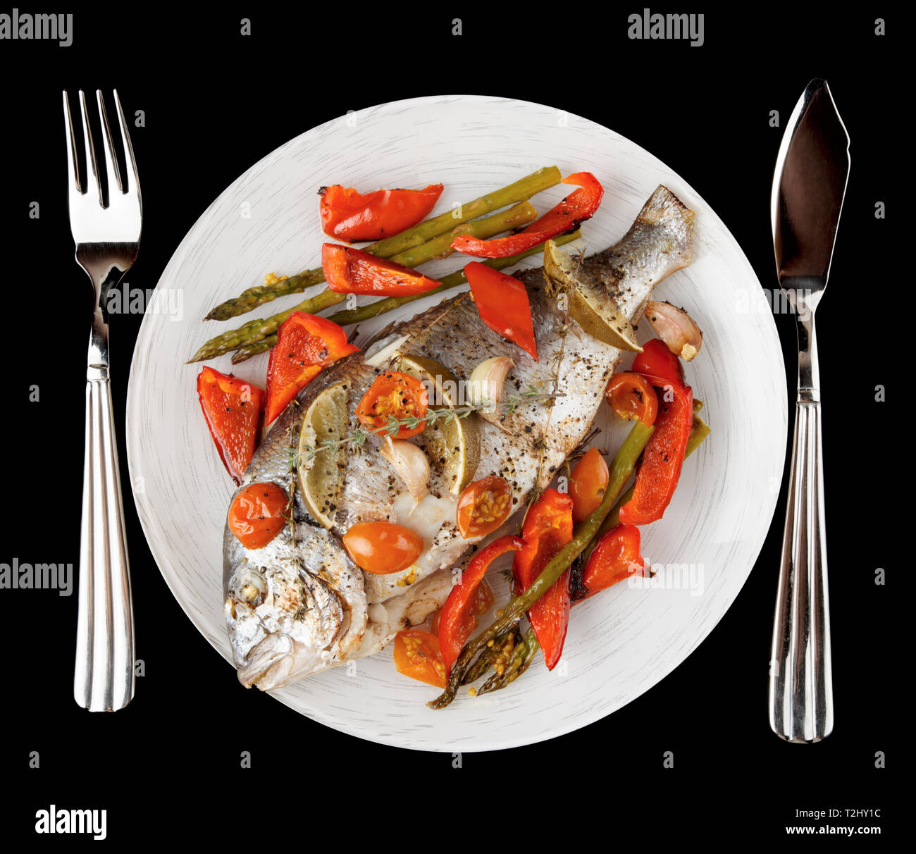Roasted gilt-head bream with vegetables on plate, isolated on black ...