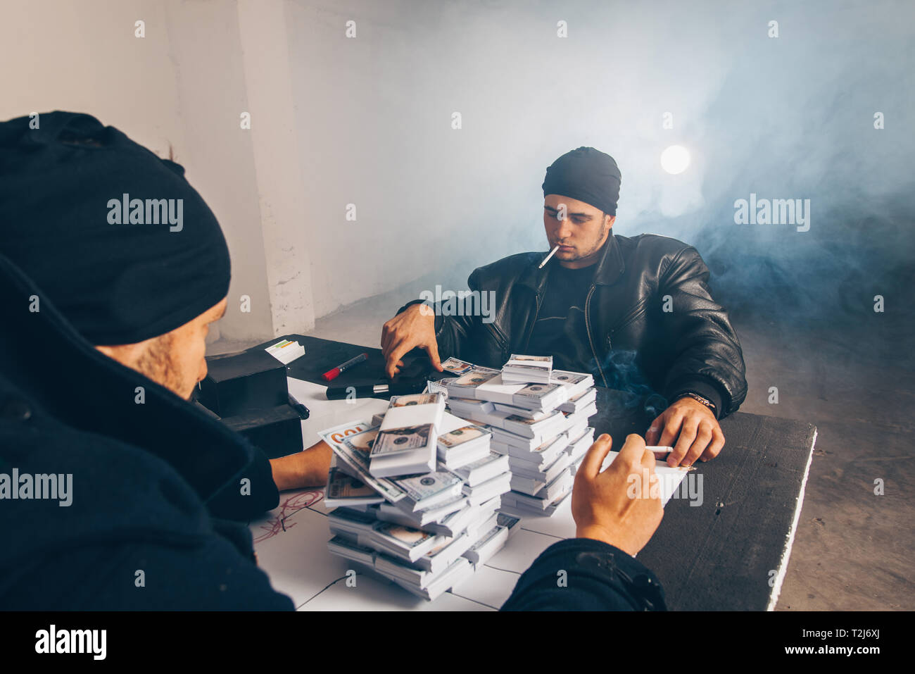 Two criminals are sitting in a dark room, talking and counting stolen ...