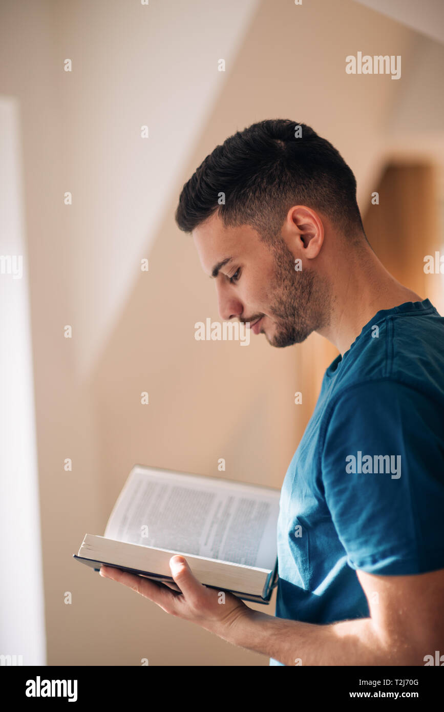 Student reading a book while standing and walking in the room next to ...