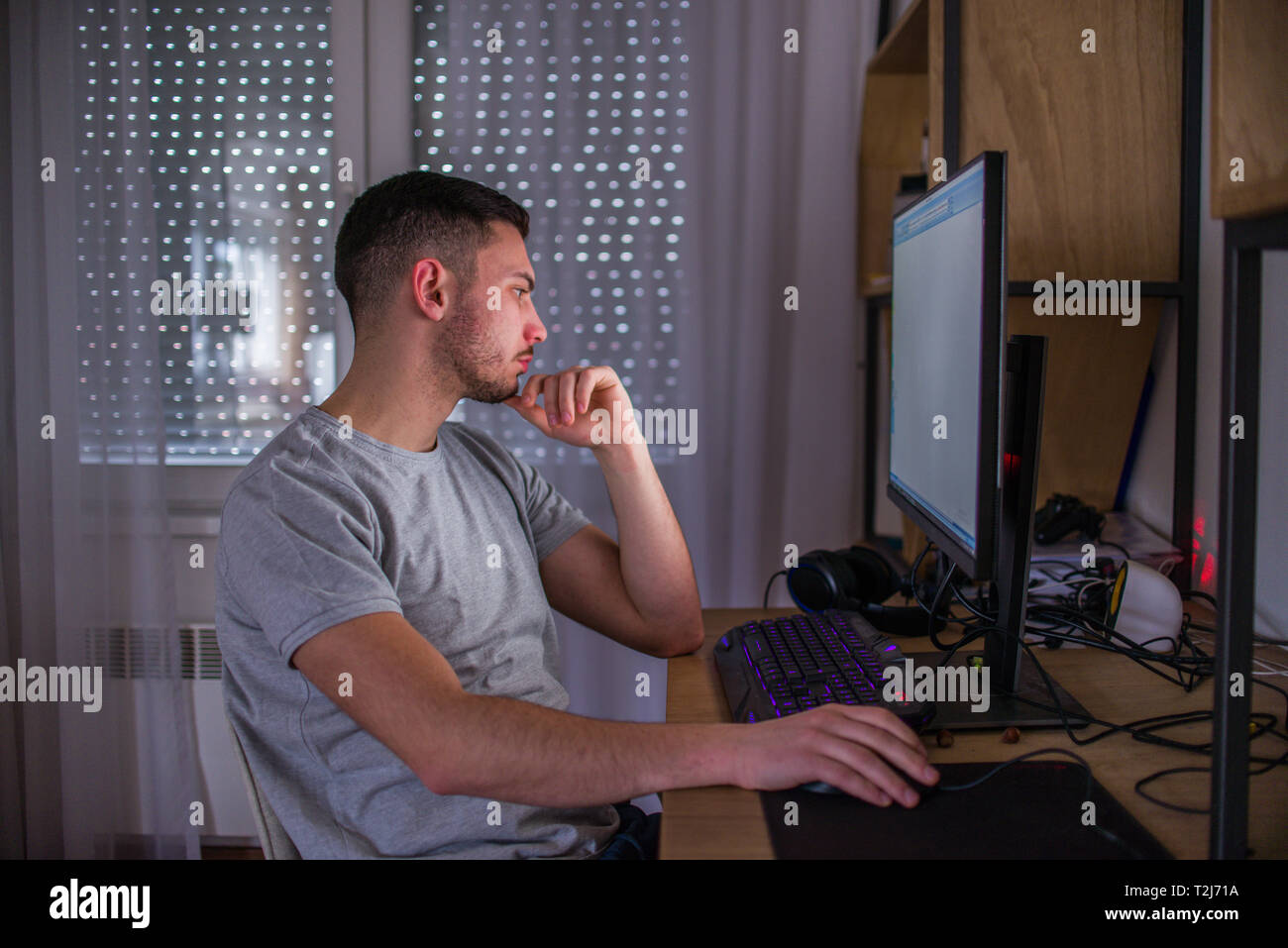 Young man looking at computer screen, working in dark room Stock Photo ...