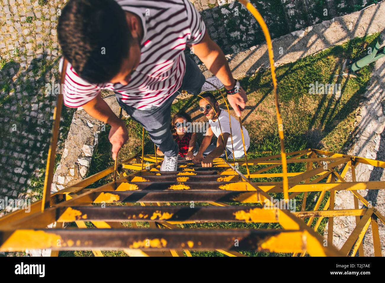 Man going front on high ladder while his two friends are on the bottom ...