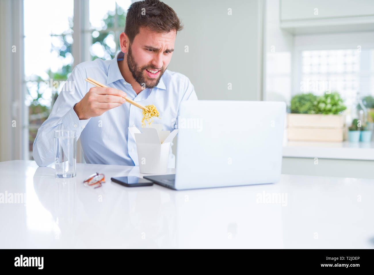 Business man eating take away asian noodles food while working using ...