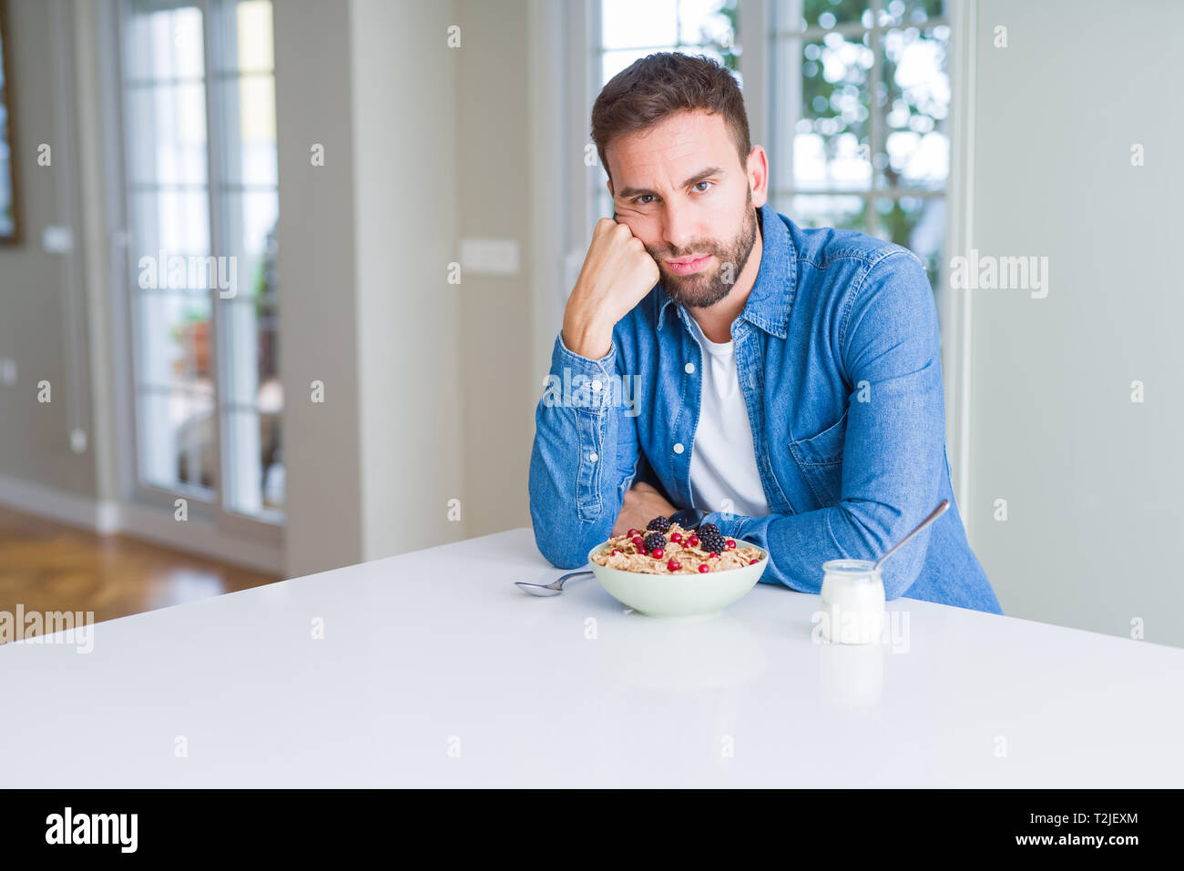 Handsome man eating cereals for breakfast at home thinking looking ...