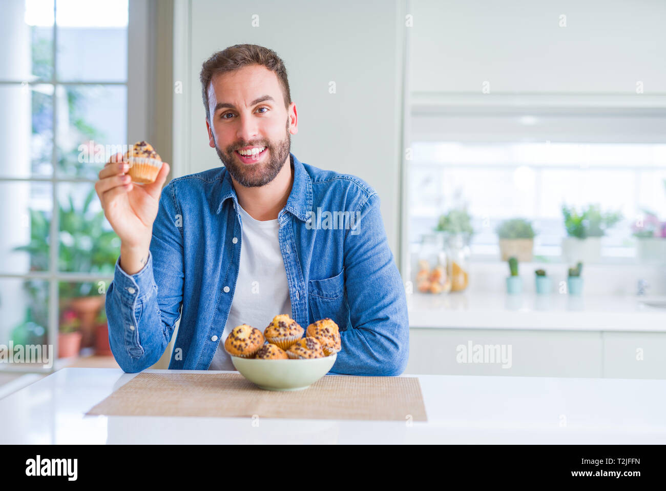Handsome man eating chocolate chips muffin with a happy face standing ...
