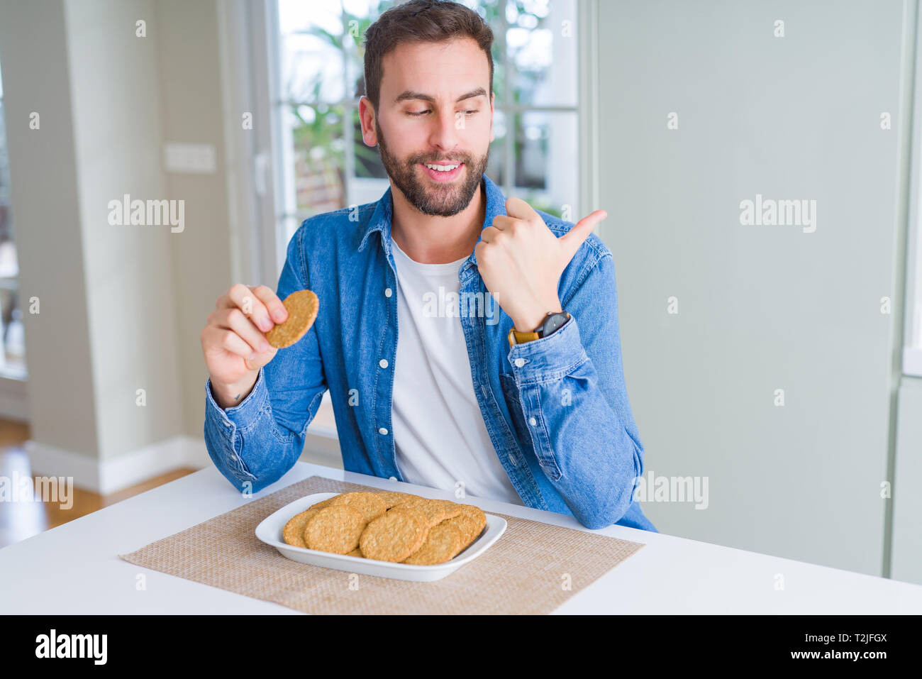 Handsome man eating healthy whole grain biscuit pointing and showing ...