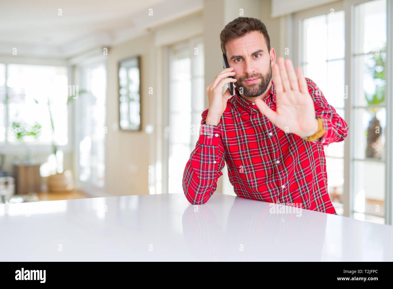 Handsome man talking on smartphone with open hand doing stop sign with ...
