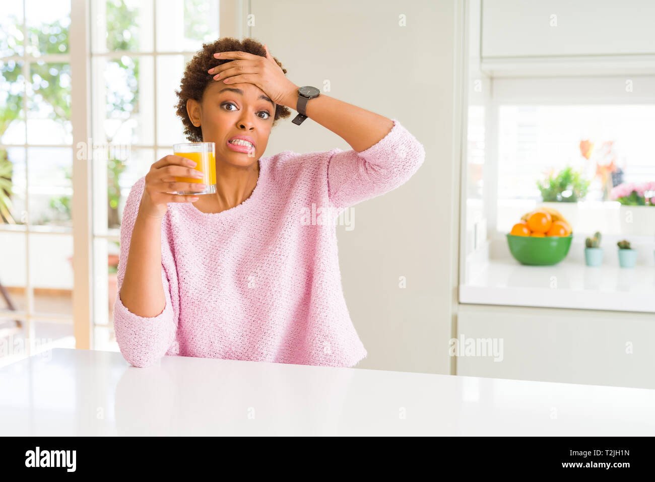 Young african american woman driking orange juice at home stressed with ...