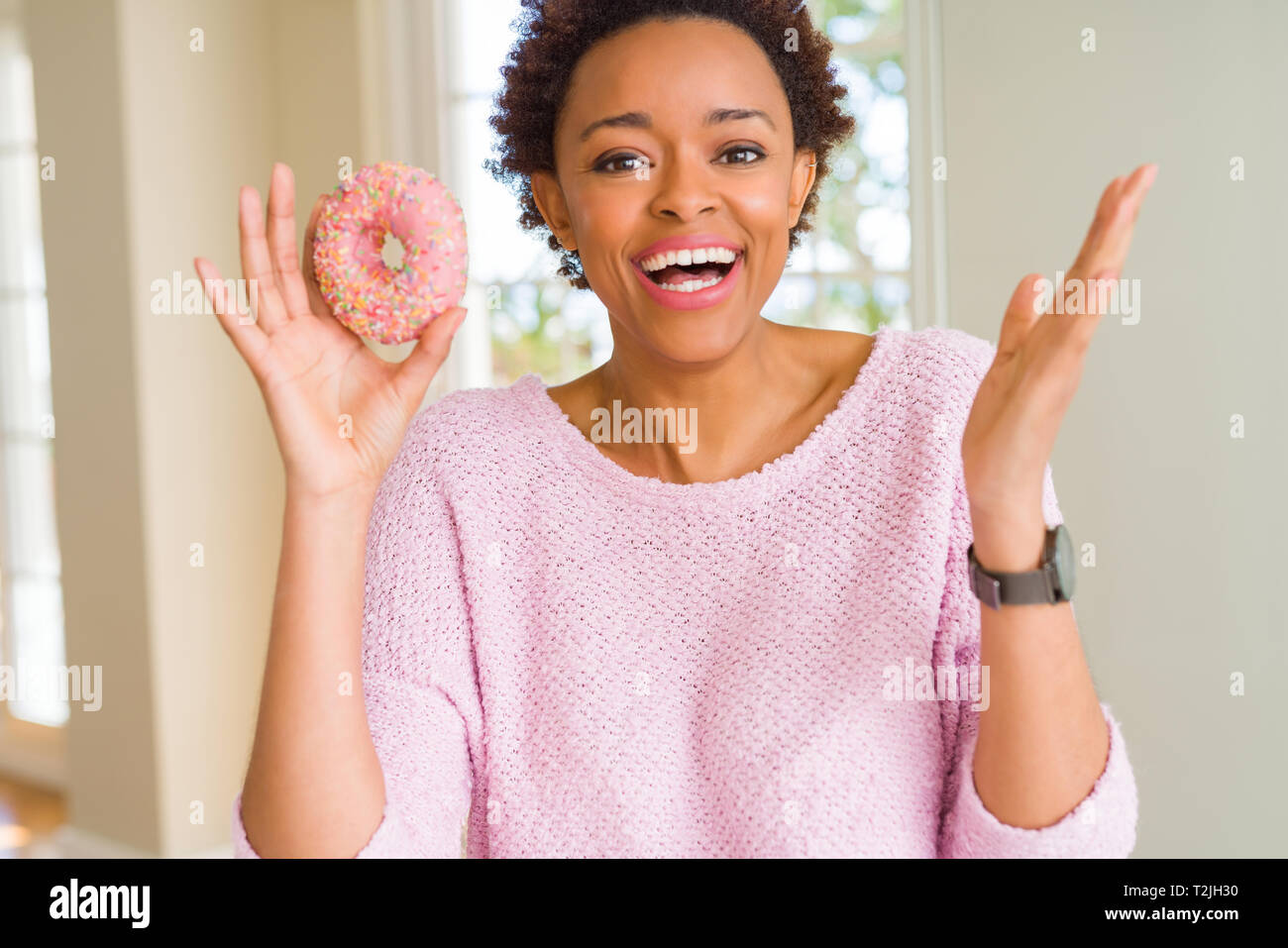 Young african american woman eating pink sugar donut very happy and ...
