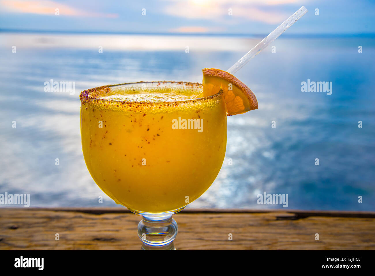 Tropical mango Cocktail by the water with an orange slaice and chili ...