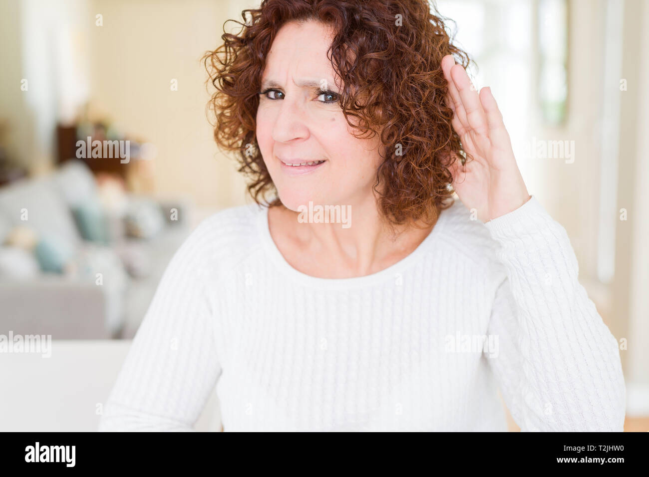 Beautiful senior woman wearing white sweater smiling with hand over ear ...
