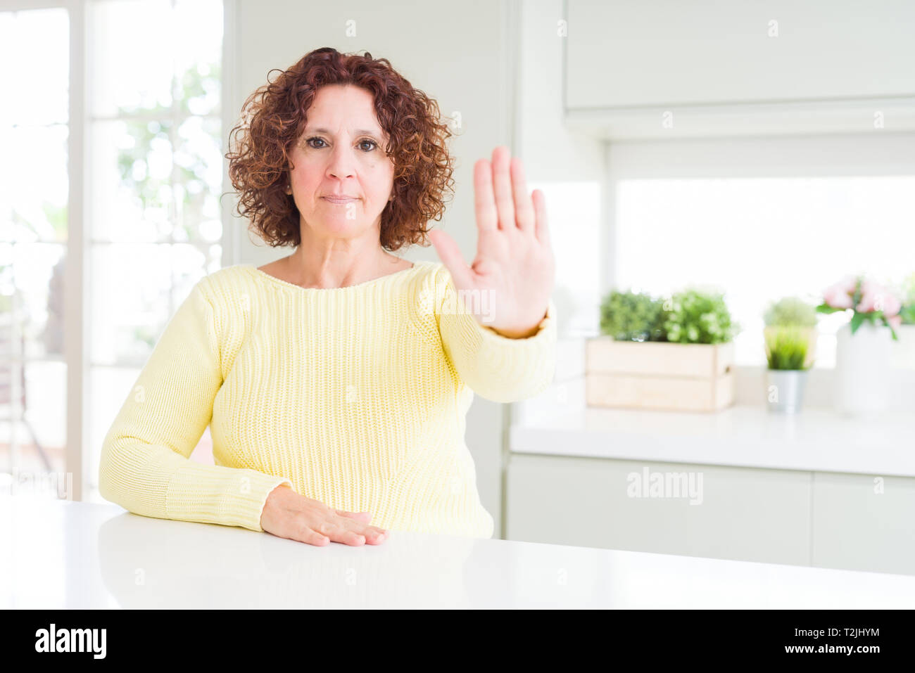 Beautiful senior woman wearing yellow sweater doing stop sing with palm ...