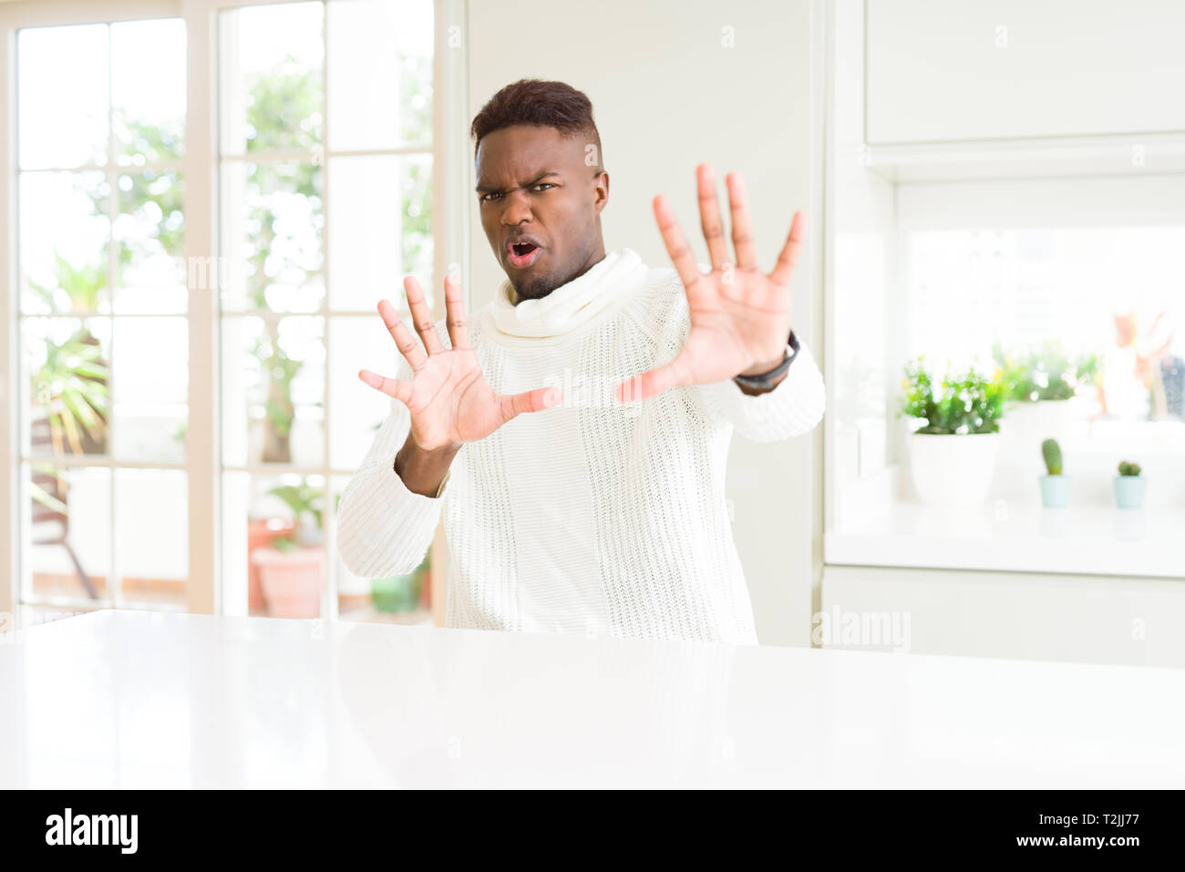 Handsome african american man on white table afraid and terrified with ...