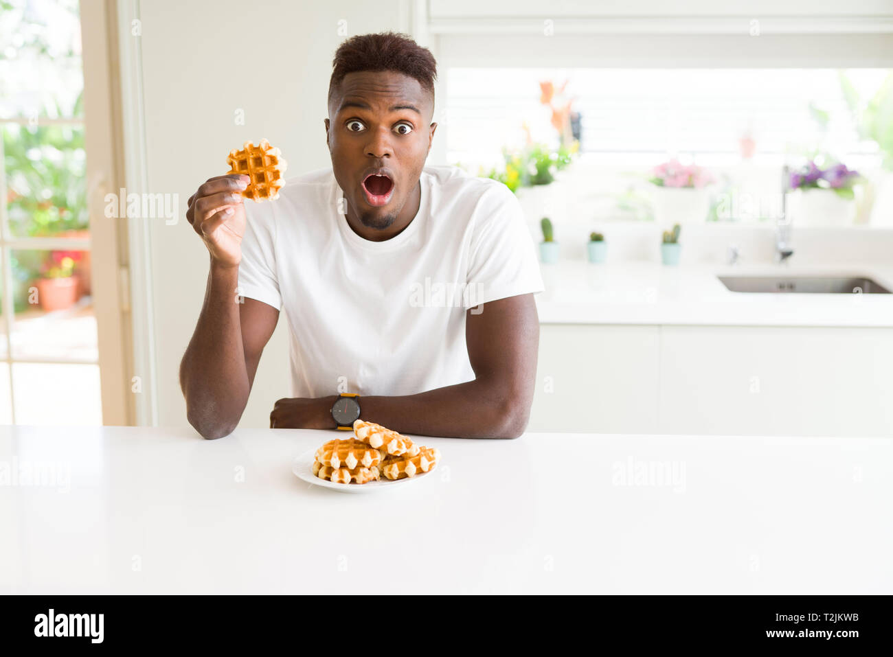African american man eating sweet Belgian waffle scared in shock with a ...