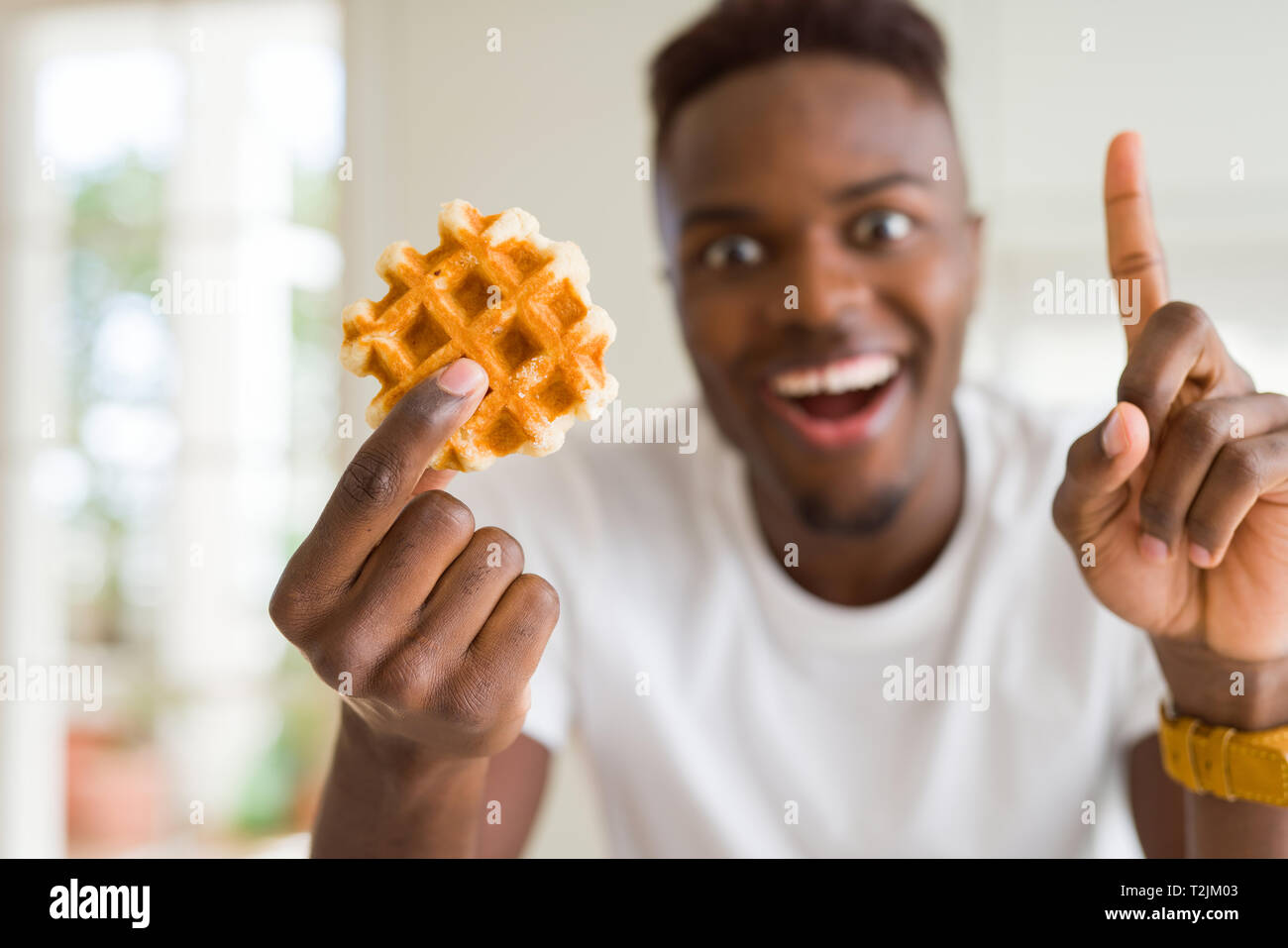 African american man eating sweet Belgian waffle surprised with an idea ...