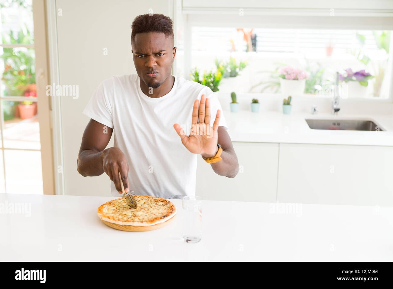 African american man eating cheese pizza at home with open hand doing ...