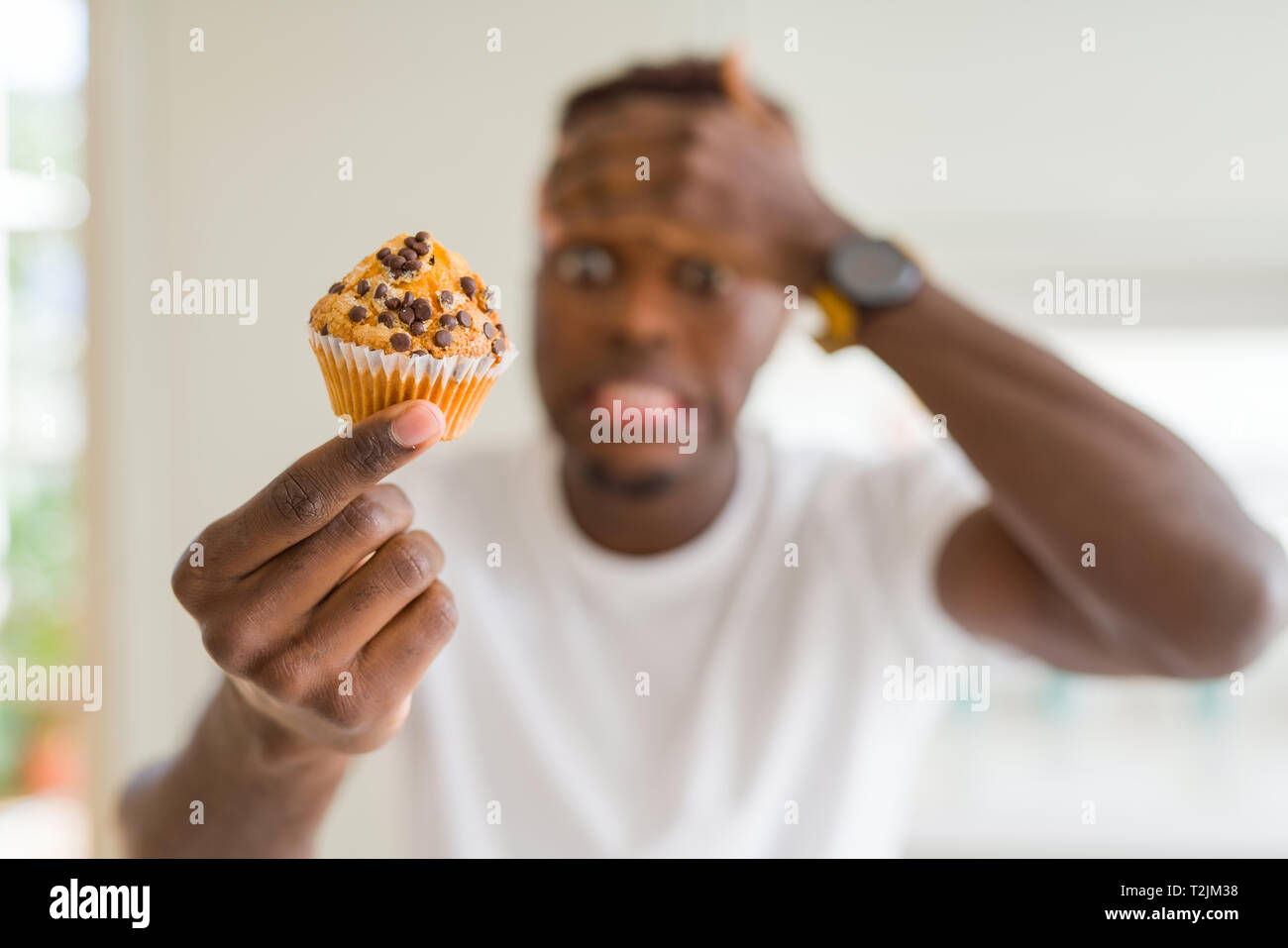 African american man eating chocolate chips muffin stressed with hand ...