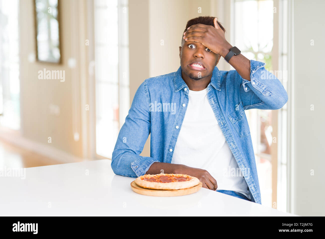 African american man eating pepperoni pizza at home stressed with hand ...