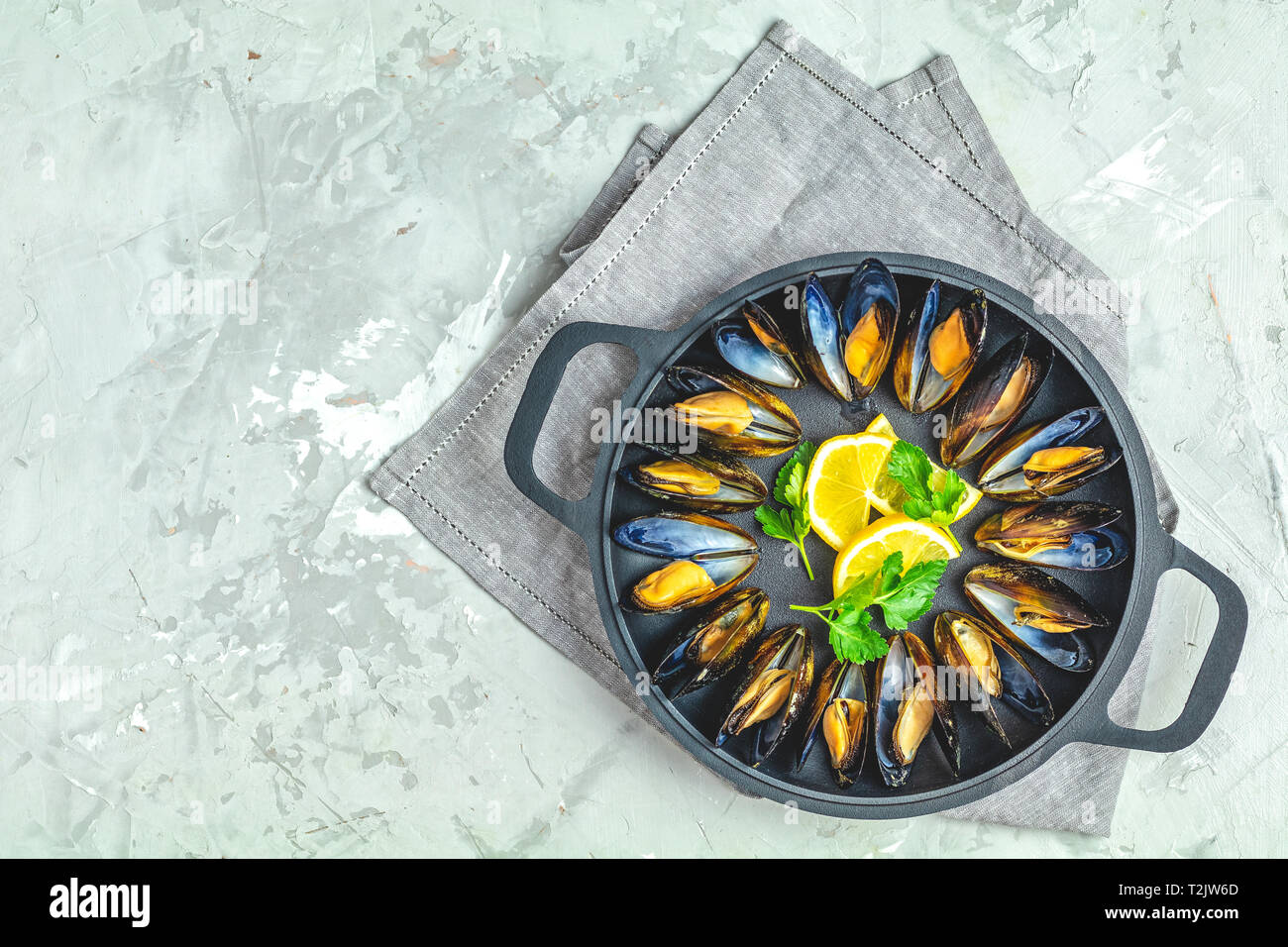 Seafood mussels with lemon and parsley in black metal pan on light gray ...