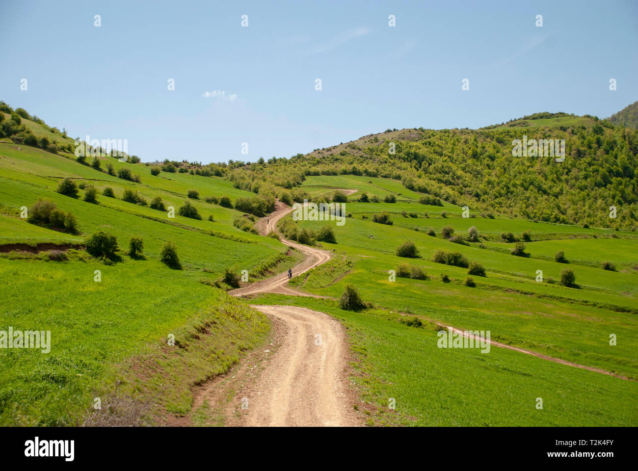A long shot of a natural green field and dirt roads and bushes and ...