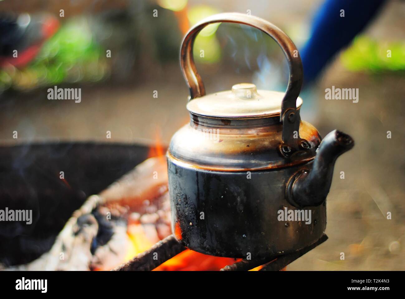 There is a water iron pot boiling on firewoods flames while smoke and ...