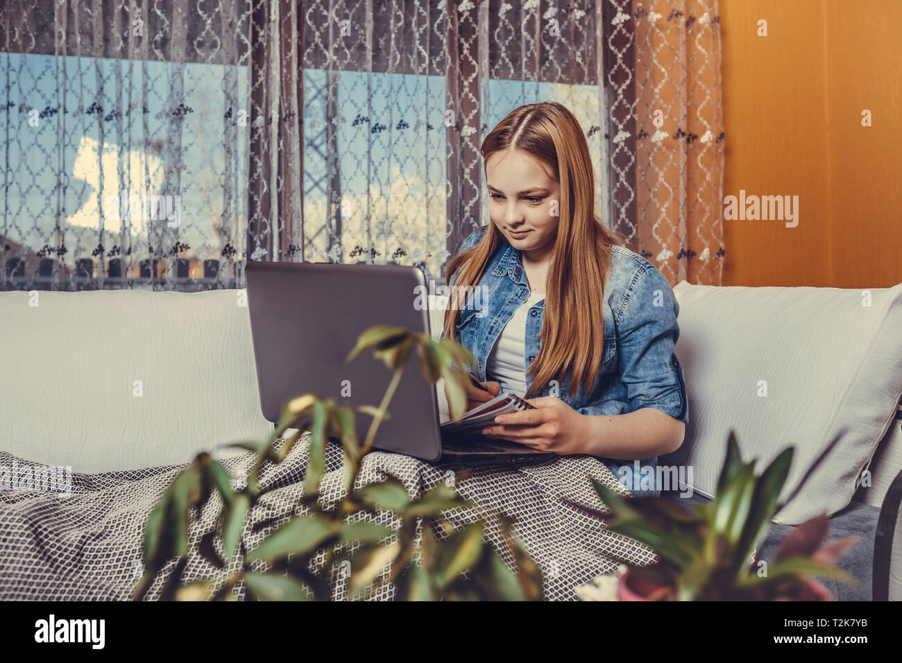 Girl sitting on a bed covered with a blanket and studying with a laptop ...