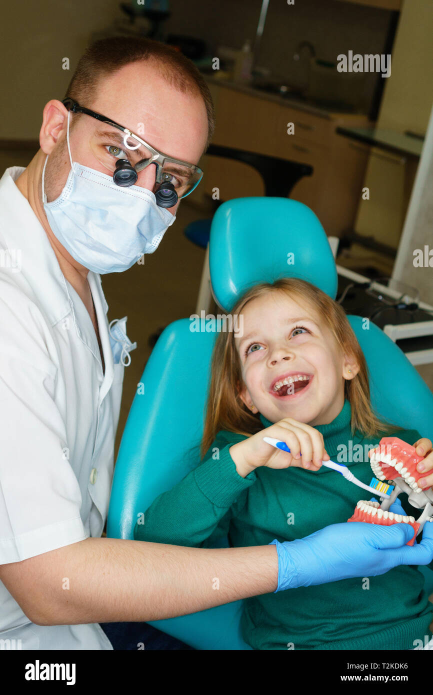 Dentist explains rules of brushing teeth to little girl, holding mock ...