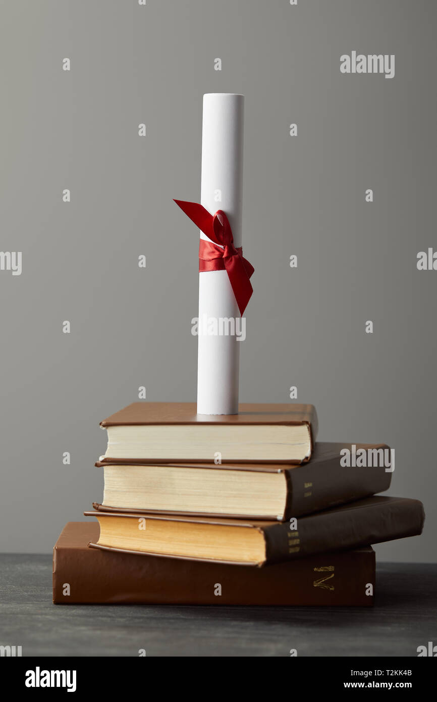 Diploma with red ribbon and books on textured surface isolated on grey ...