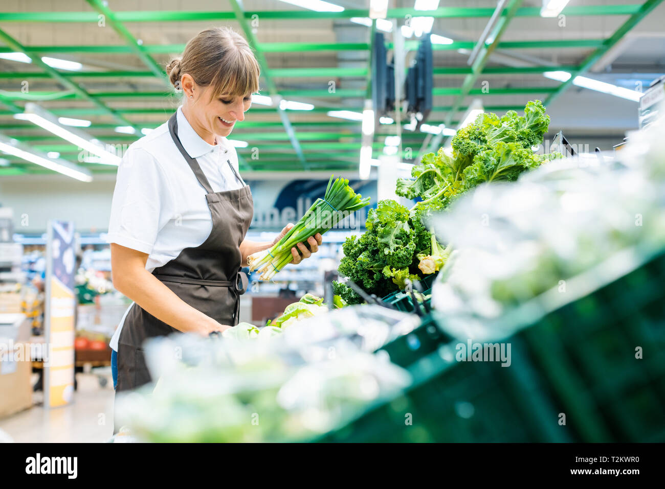 Shop assistant in supermarket re-stocking fresh vegetables into boxes ...