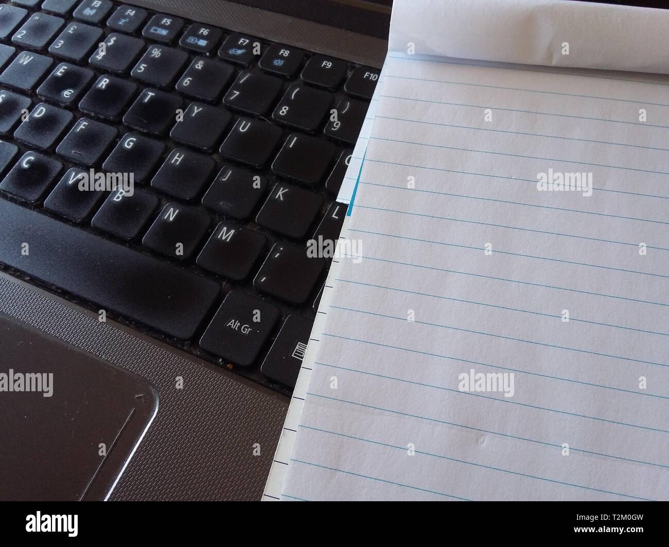 Detail of laptop, black, next to it a notebook a white open page in ...
